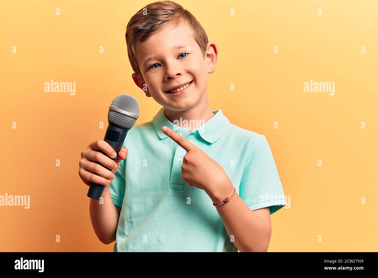 Cute blond kid singing song using microphone smiling happy pointing ...