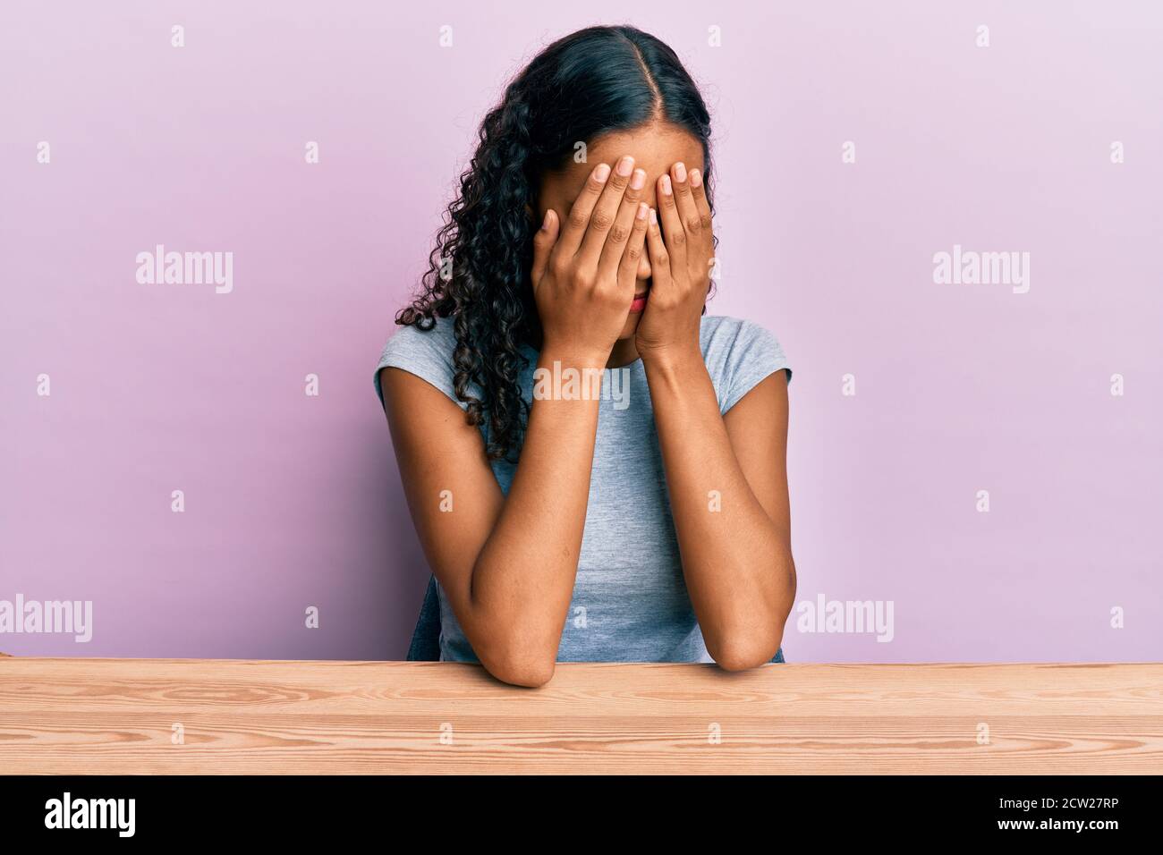 Young african american girl wearing casual clothes sitting on the table ...
