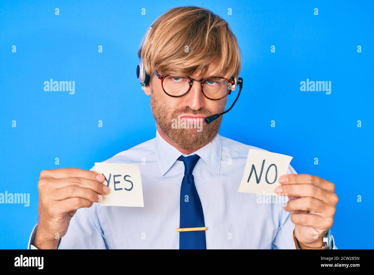 Young blond man wearing operator headset holding yes and no reminder ...