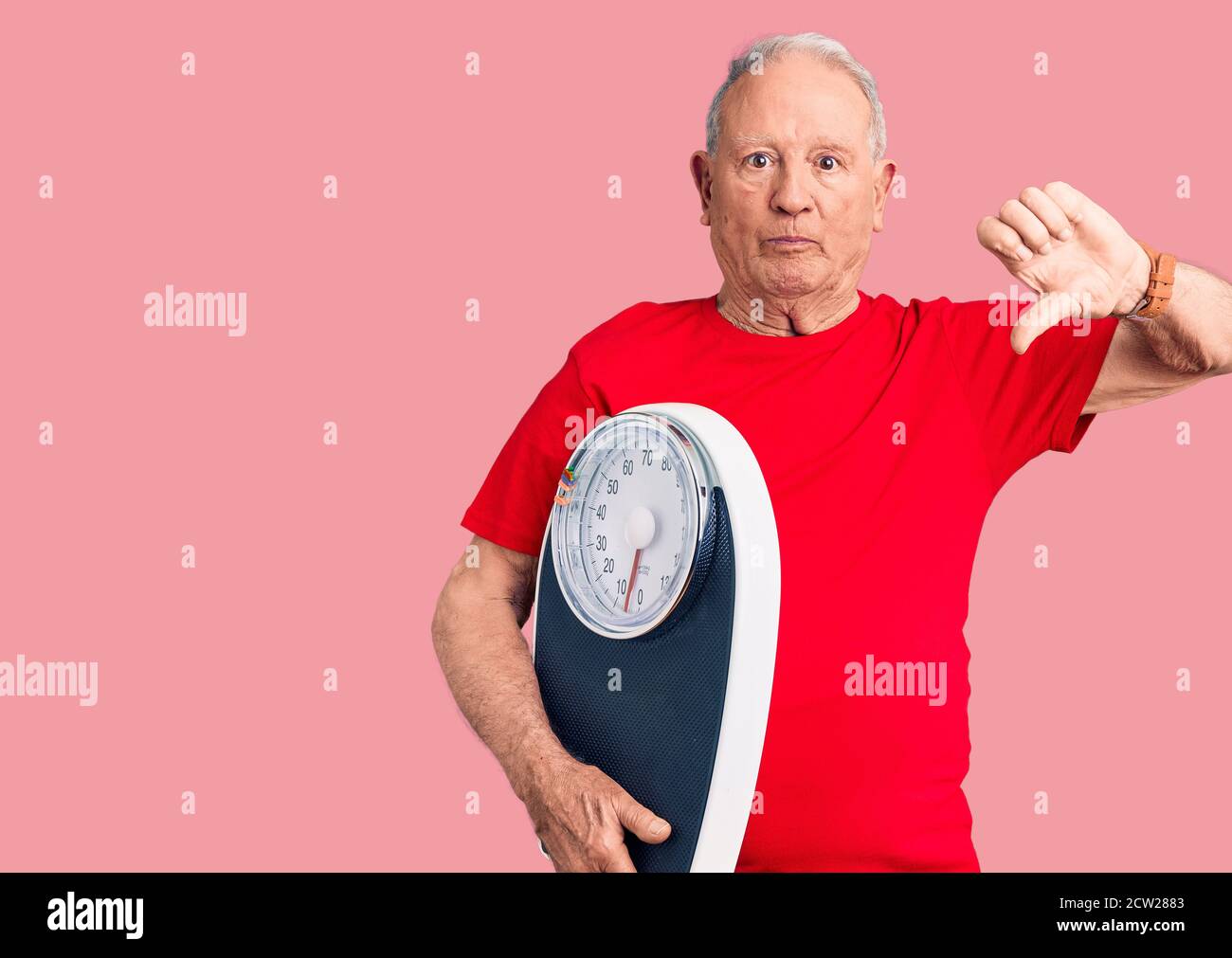 Senior handsome grey-haired man holding weighing machine with angry ...