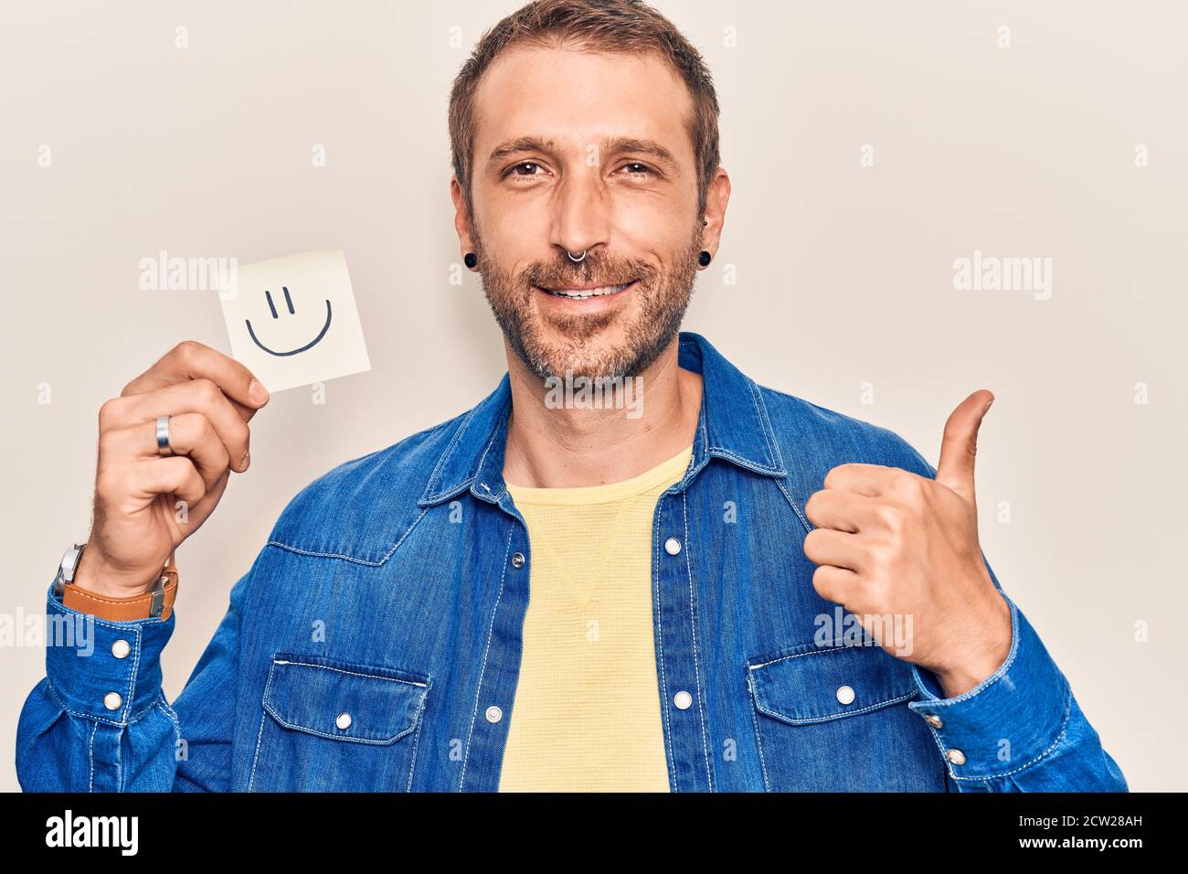 Young handsome man holding smile emoji reminder smiling happy and ...