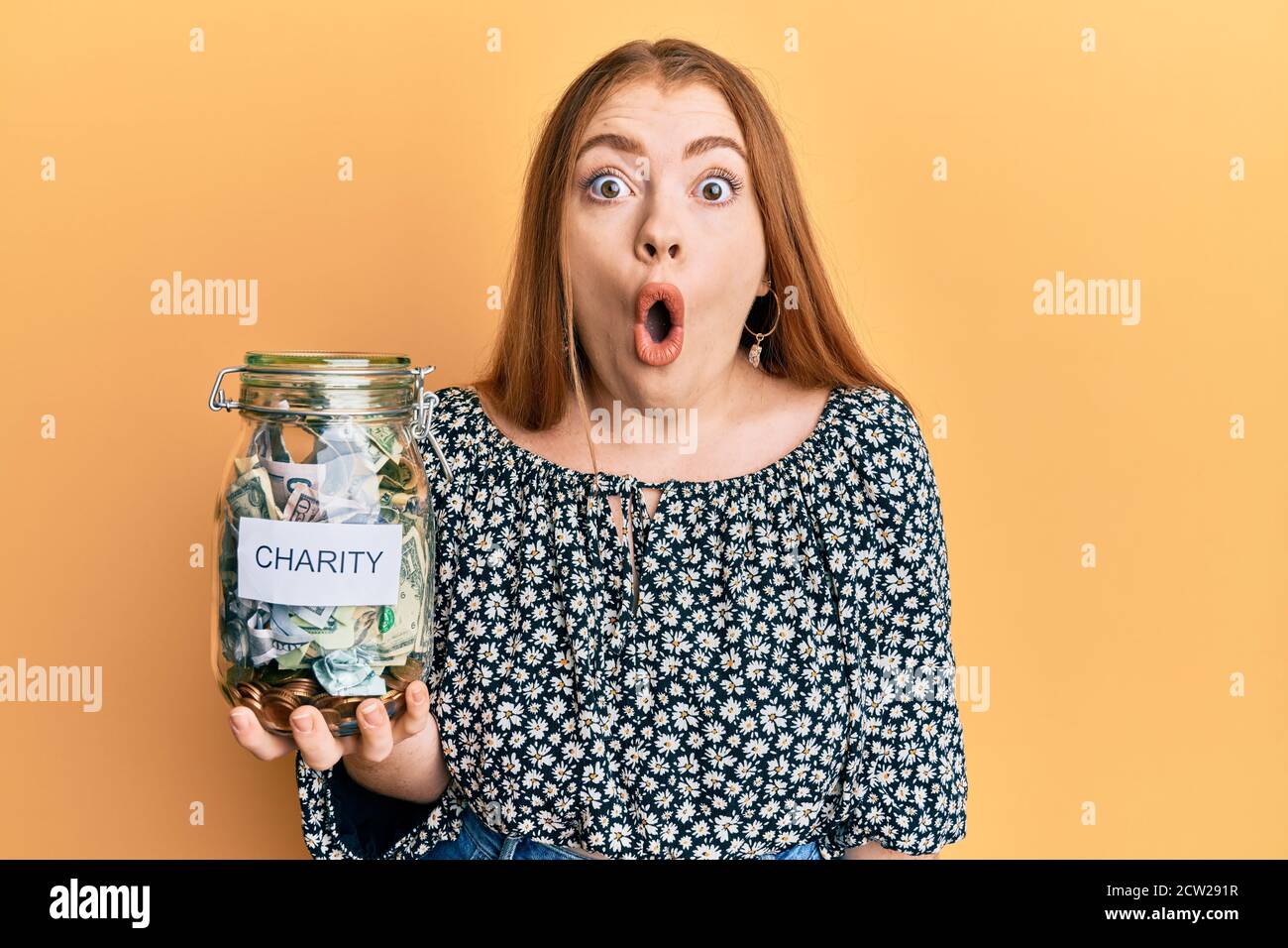 Young beautiful redhead woman holding charity jar with money scared and ...