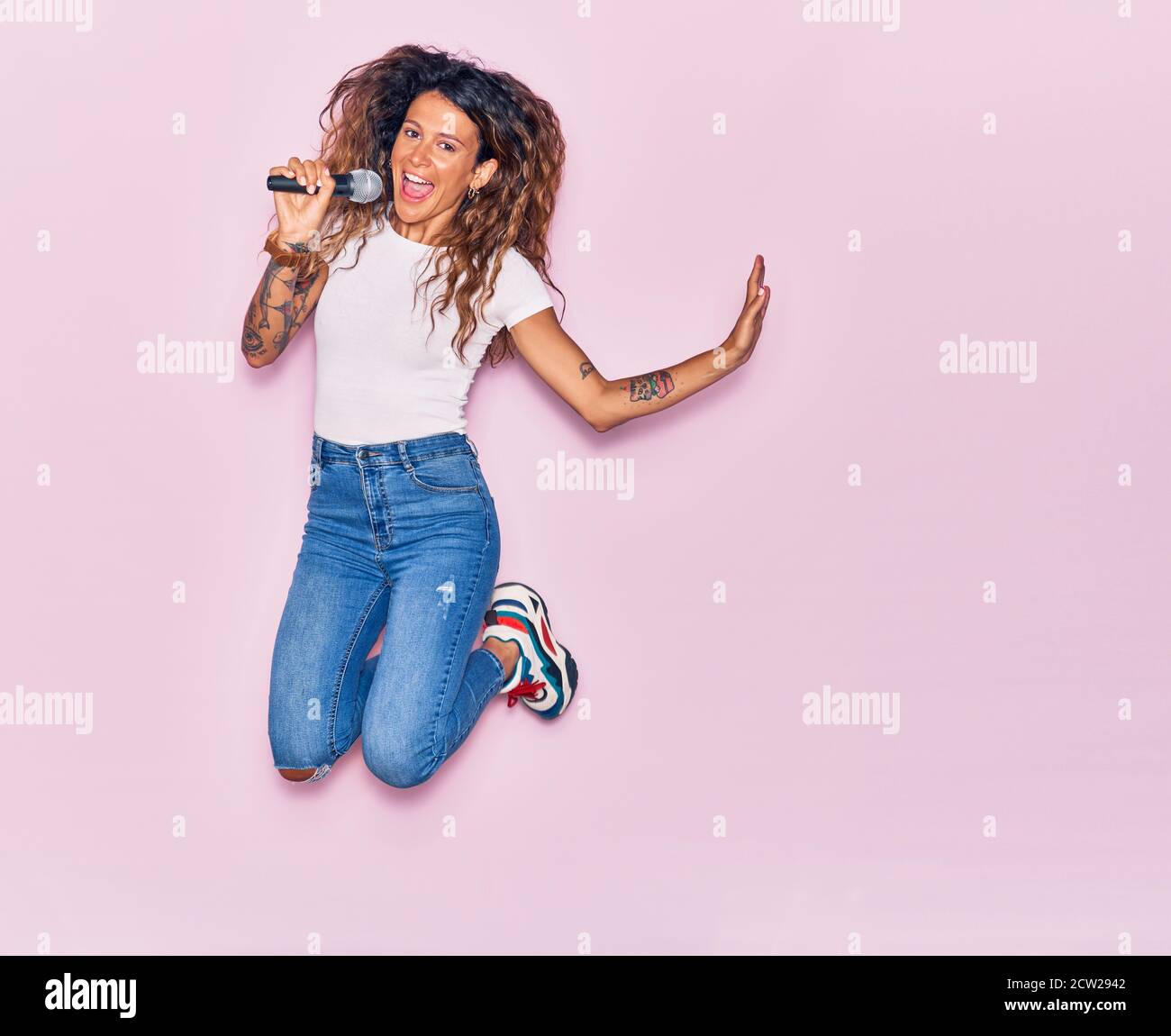 Young beautiful curly singer woman with tattoo smiling happy. Jumping ...