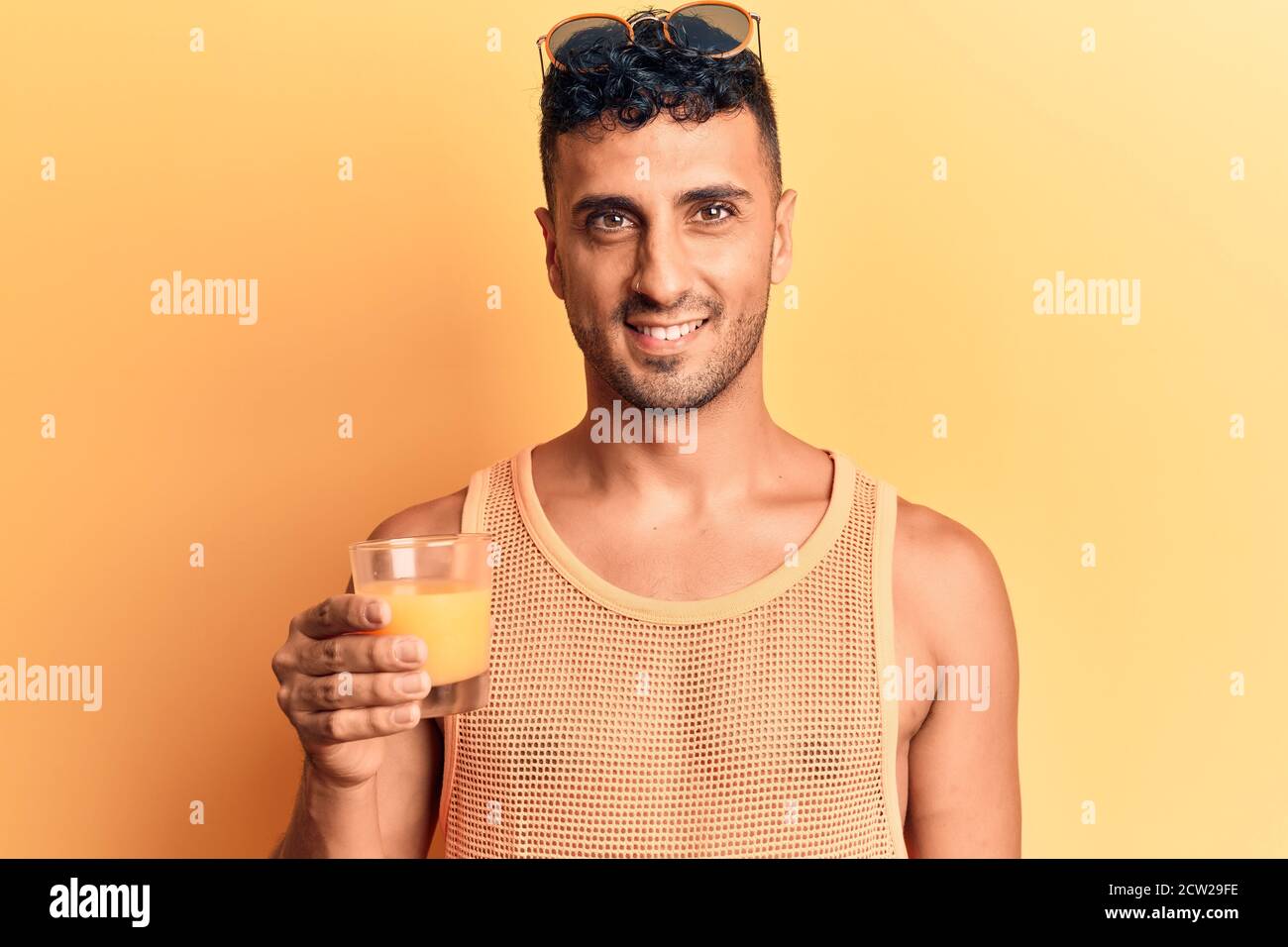 Young hispanic man drinking glass of orange juice looking positive and ...