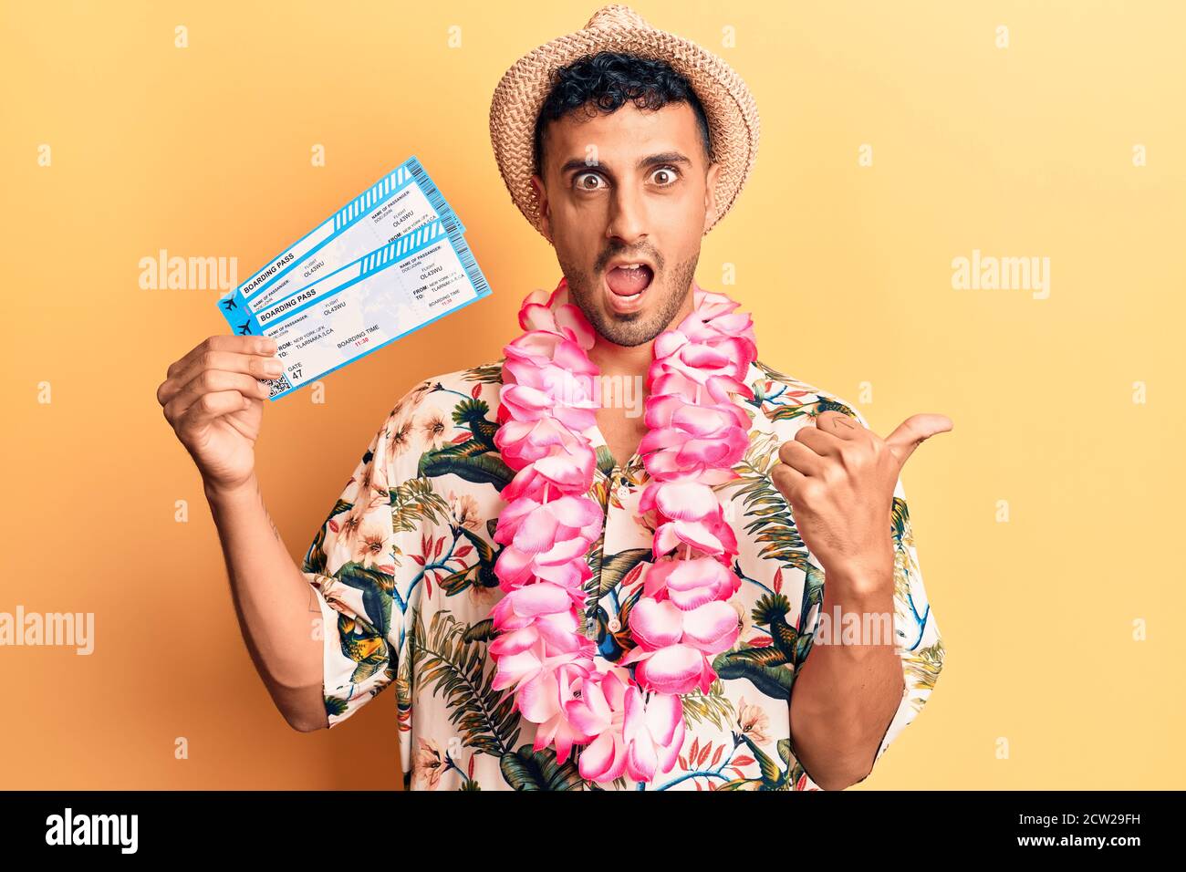 Young hispanic man wearing summer hat holding boarding pass pointing ...