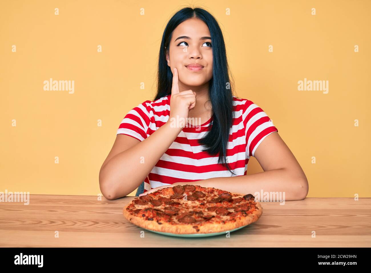 Young beautiful asian girl eating tasty pepperoni pizza serious face ...