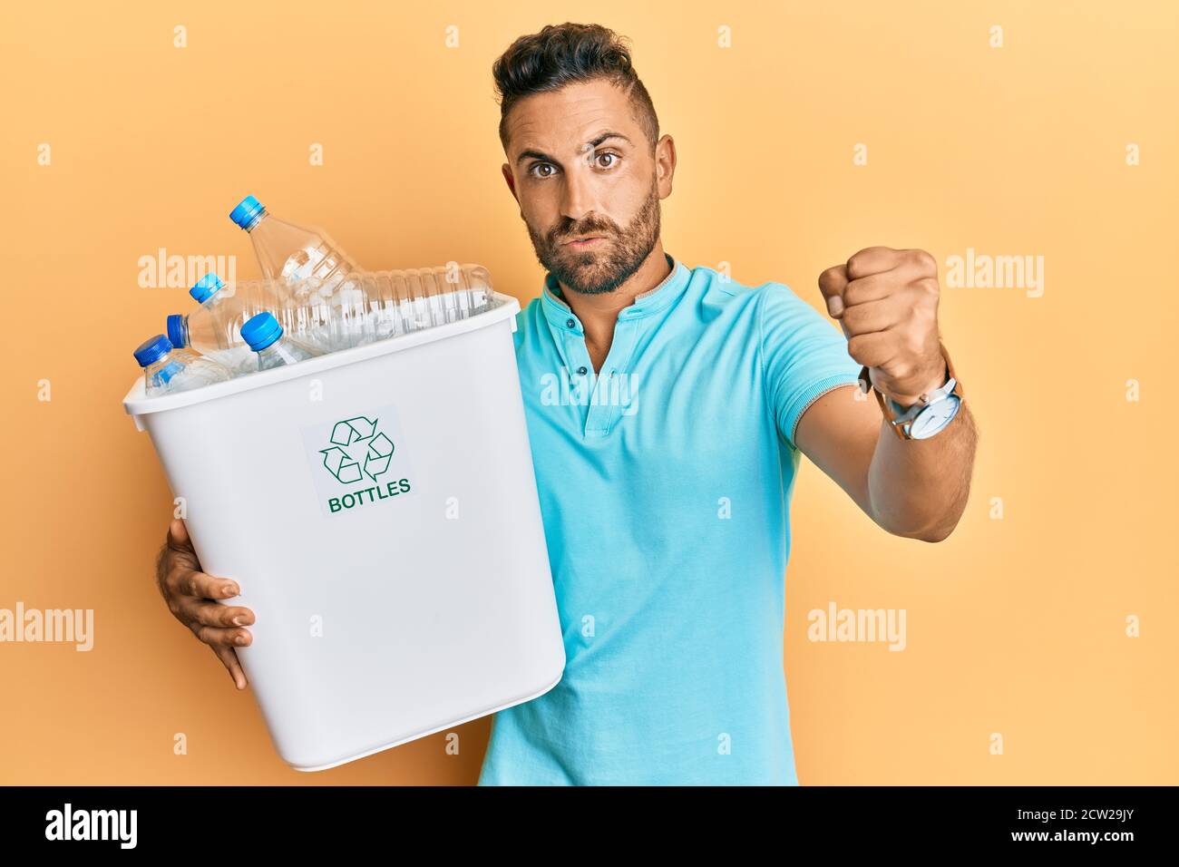 Handsome man with beard holding recycling wastebasket with plastic ...