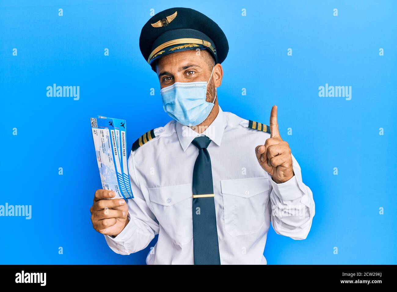 Handsome pilot man with beard wearing safety mask holding boarding pass ...