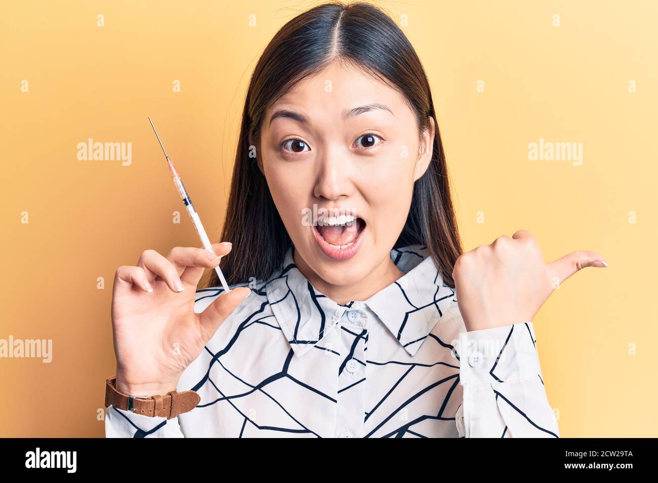 Young beautiful chinese woman holding syringe pointing thumb up to the ...