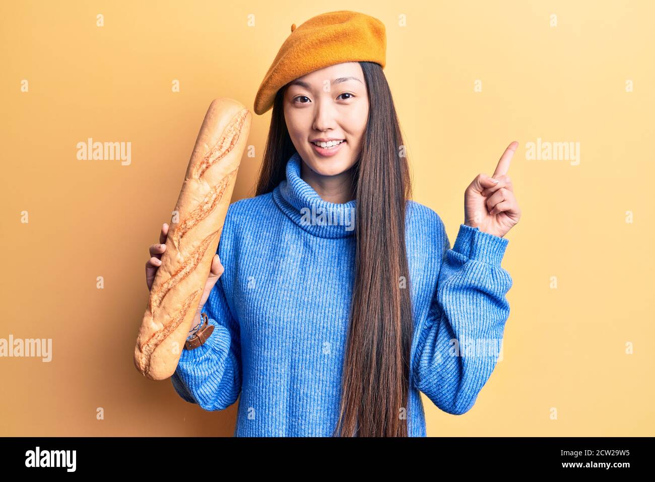 Young beautiful blonde woman wearing french beret holding bread smiling ...