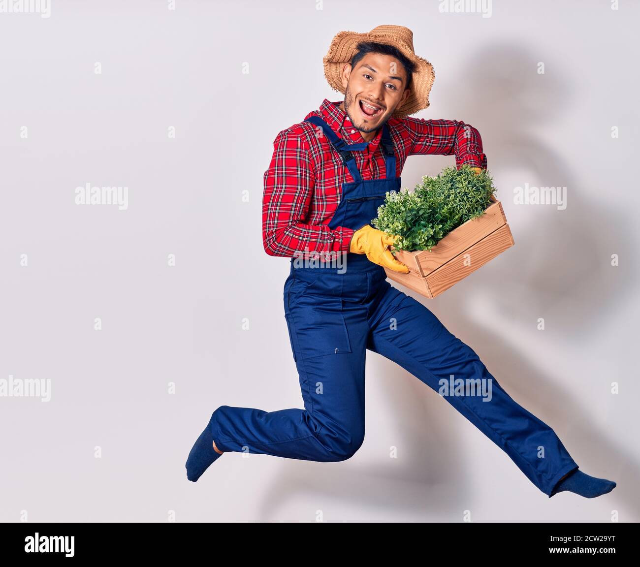Young handsome latin man wearing farmer uniform and hat smiling happy ...