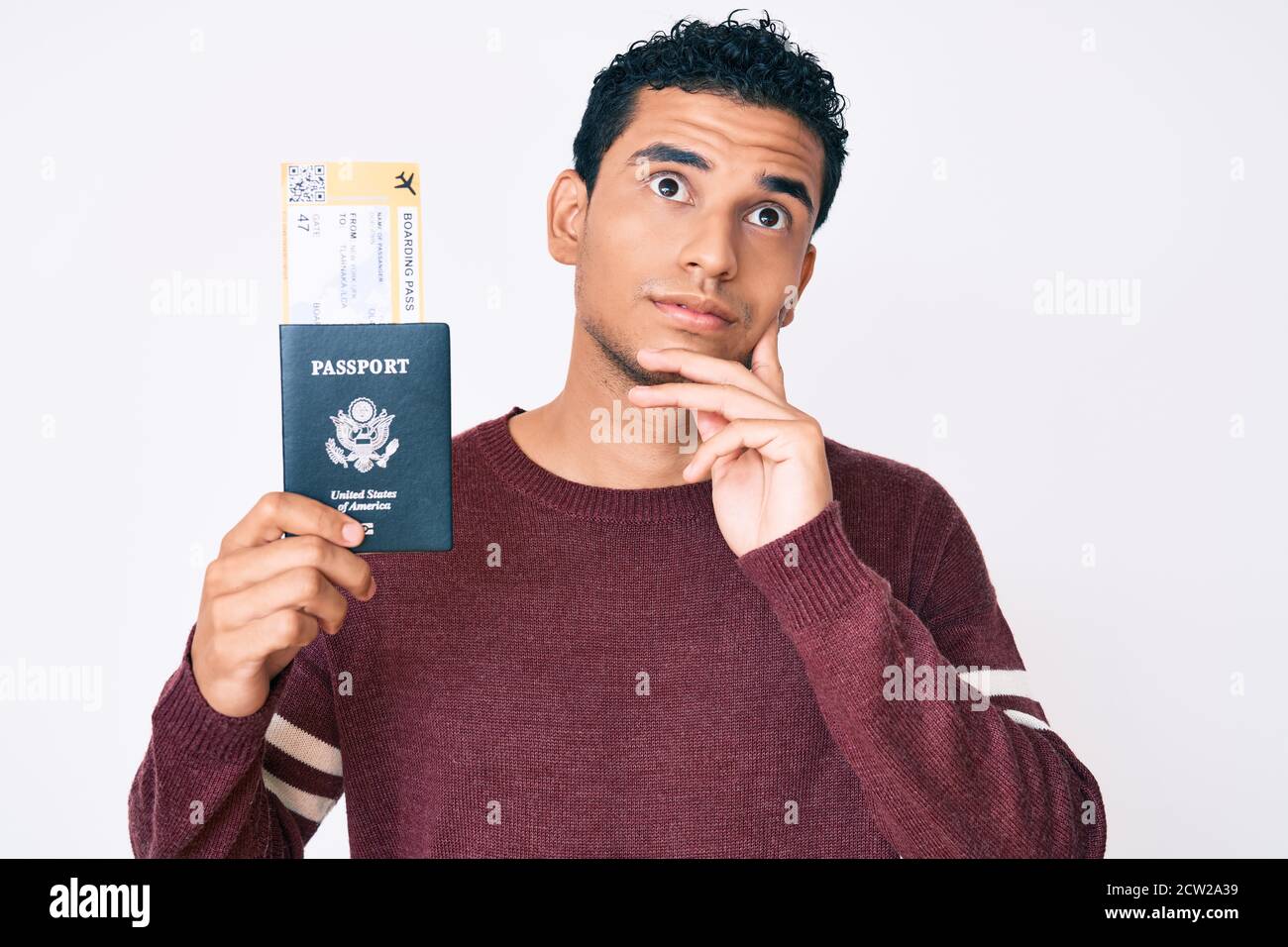 Young handsome hispanic man holding boarding pass and passport serious ...