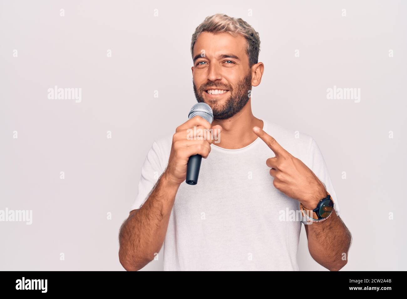 Handsome blond singer man with beard singing song using microphone over white background smiling ...
