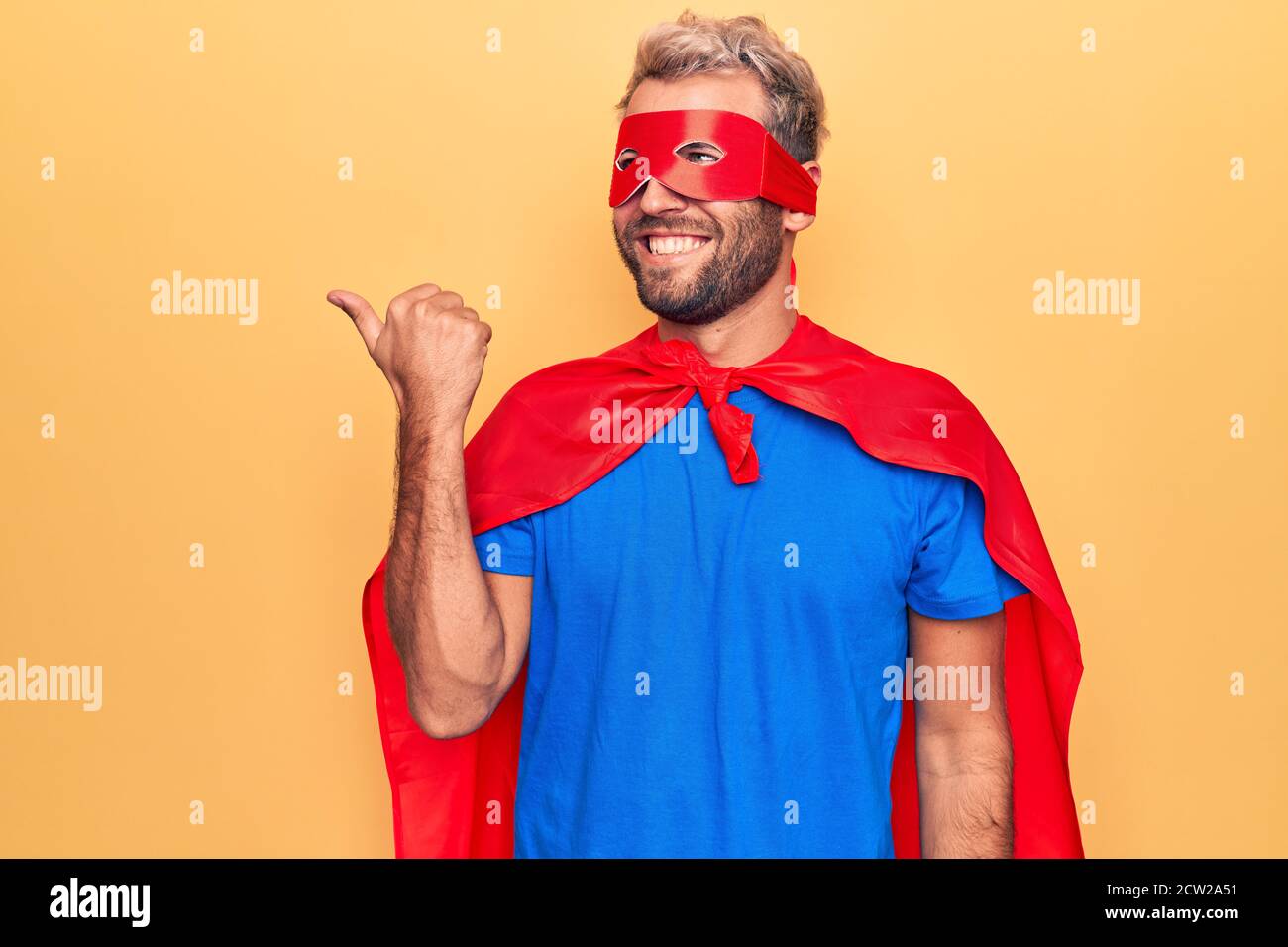 Handsome blond man wearing super hero costume with mask and cape over ...