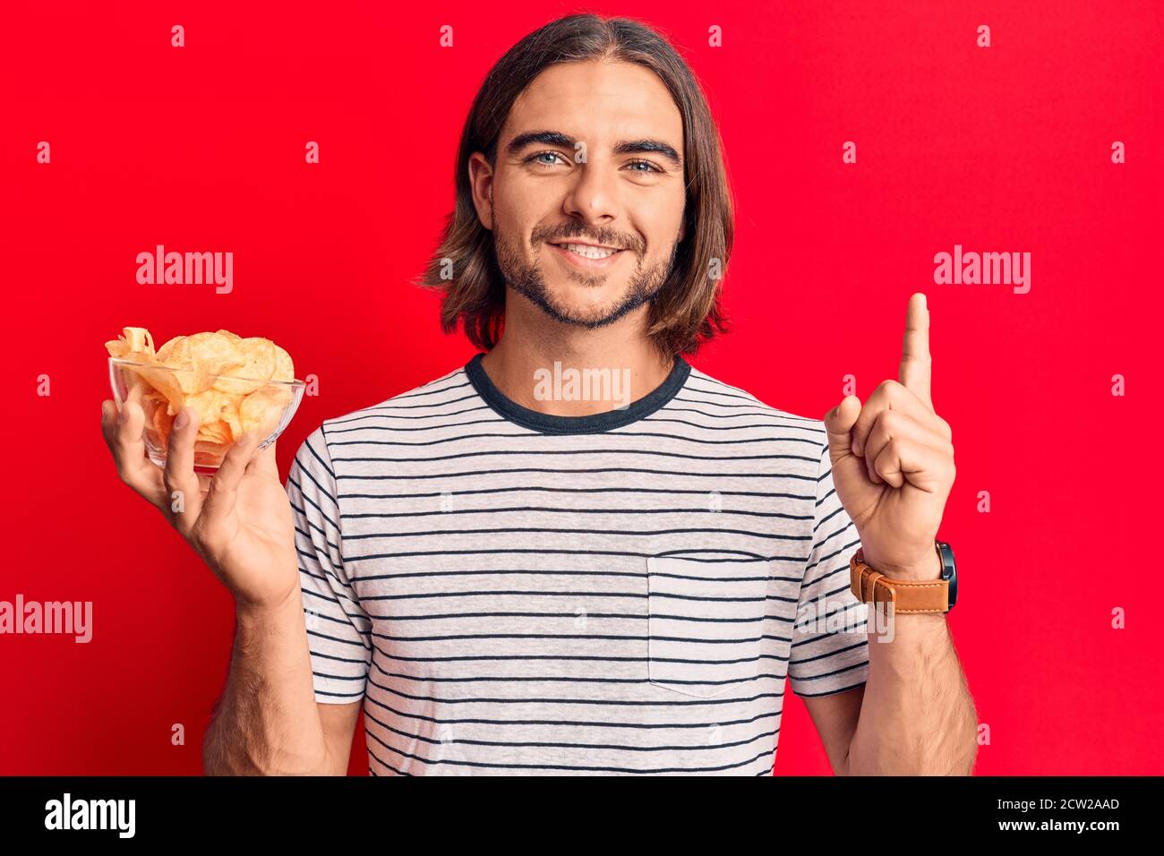 Young handsome man holding potato chip surprised with an idea or ...