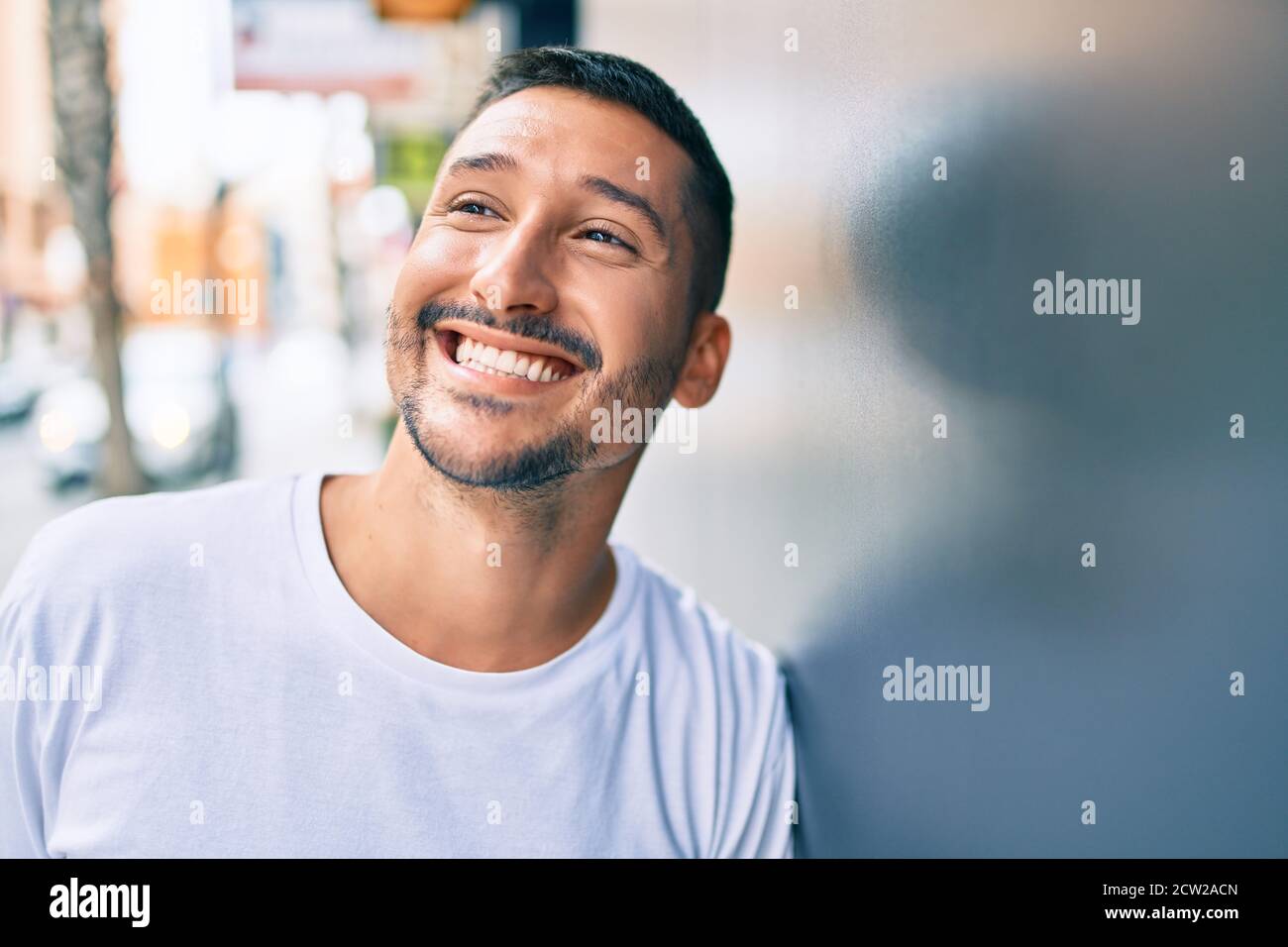Young hispanic man smiling happy leaning on the wall at street of city ...