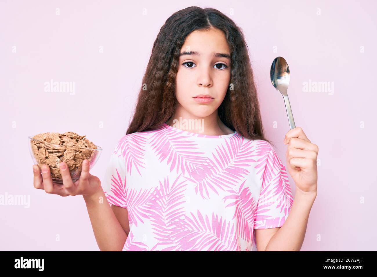 Cute hispanic girl holding cornflakes and spoon depressed and worry for ...