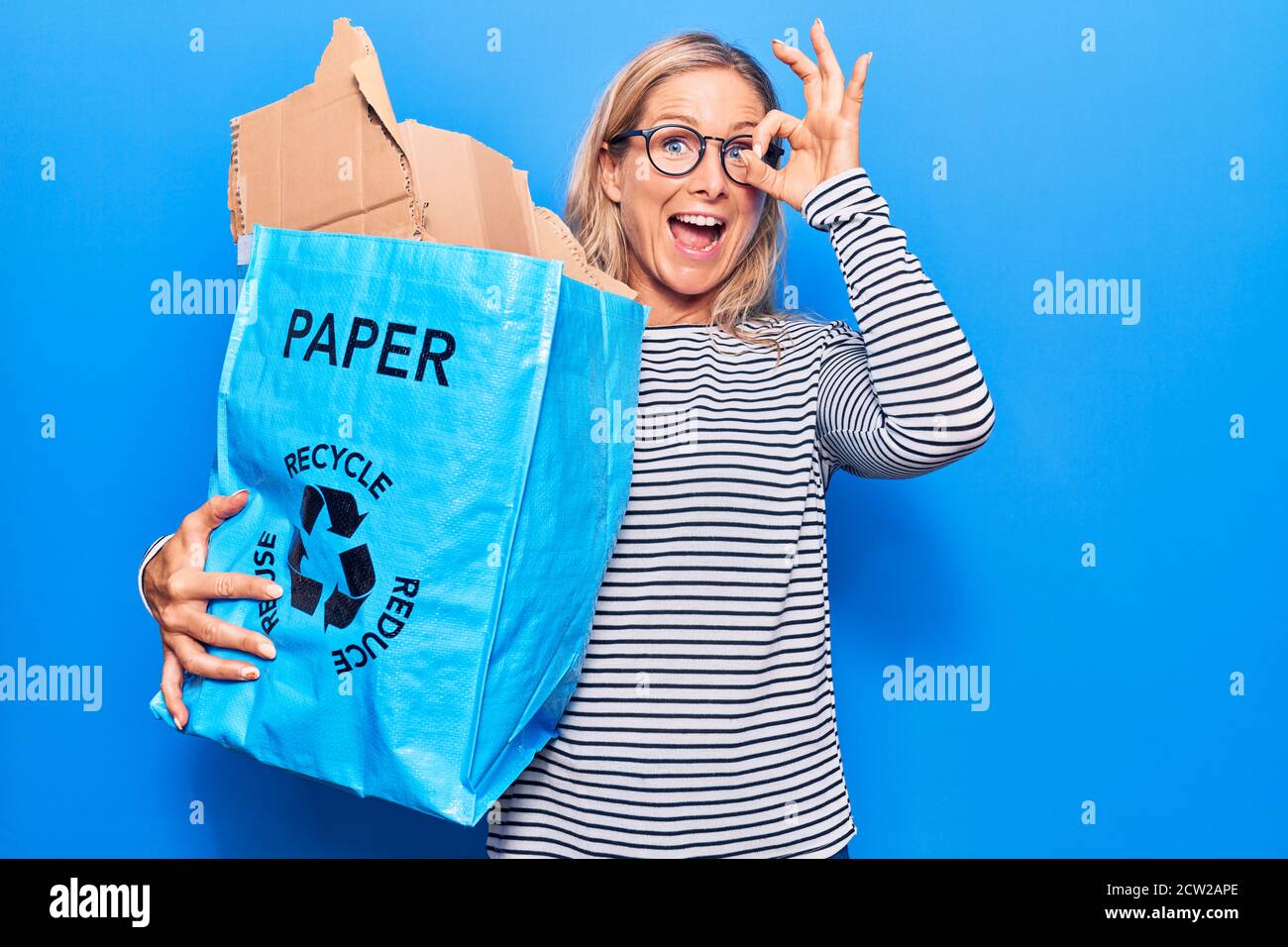 Middle age caucasian blonde woman holding recycling wastebasket with ...