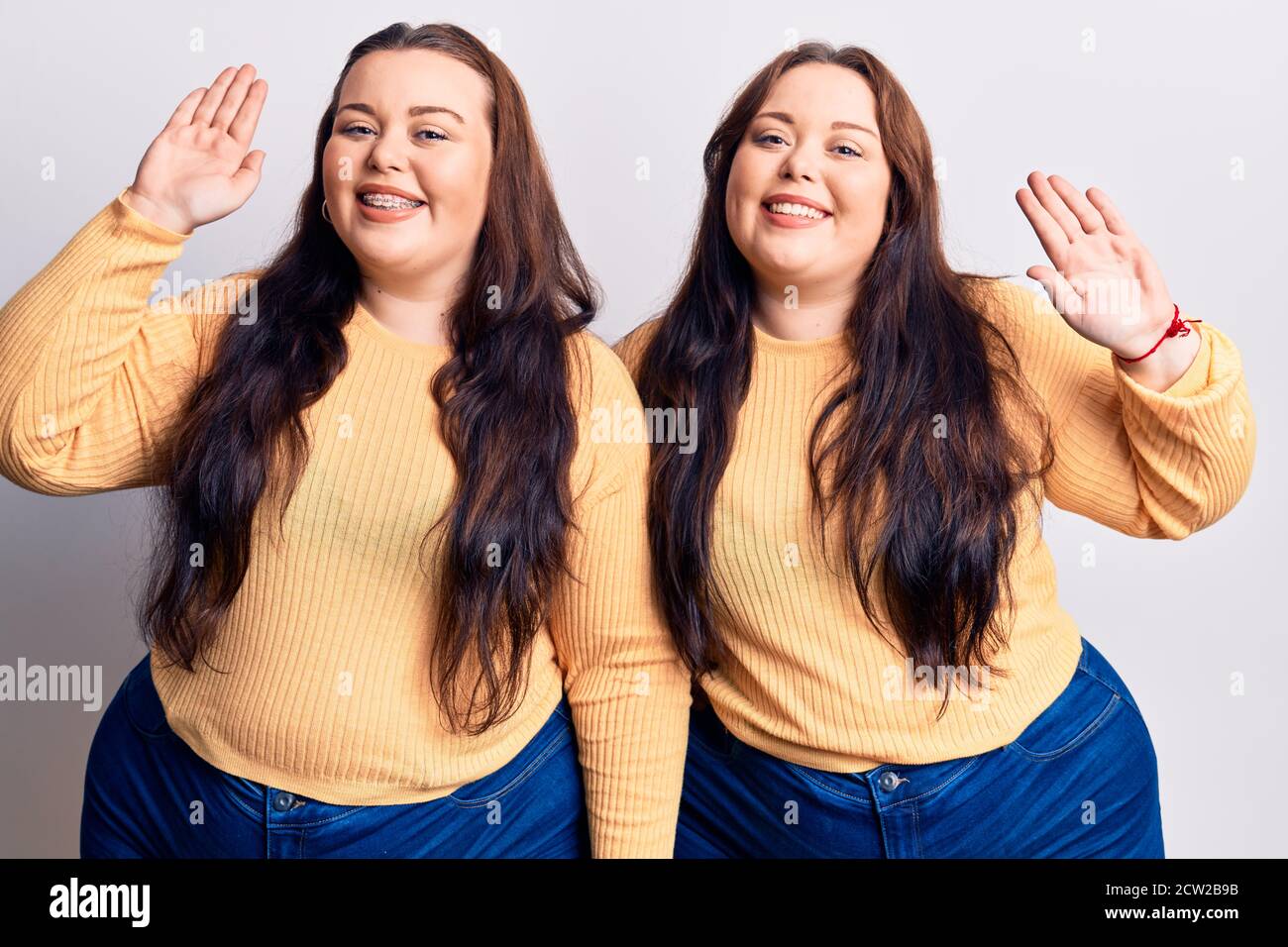 Young plus size twins wearing casual clothes waiving saying hello happy ...