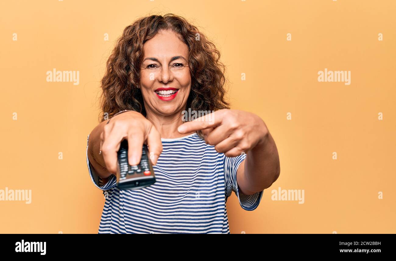 Middle age beautiful woman changing tv channel using television remote ...