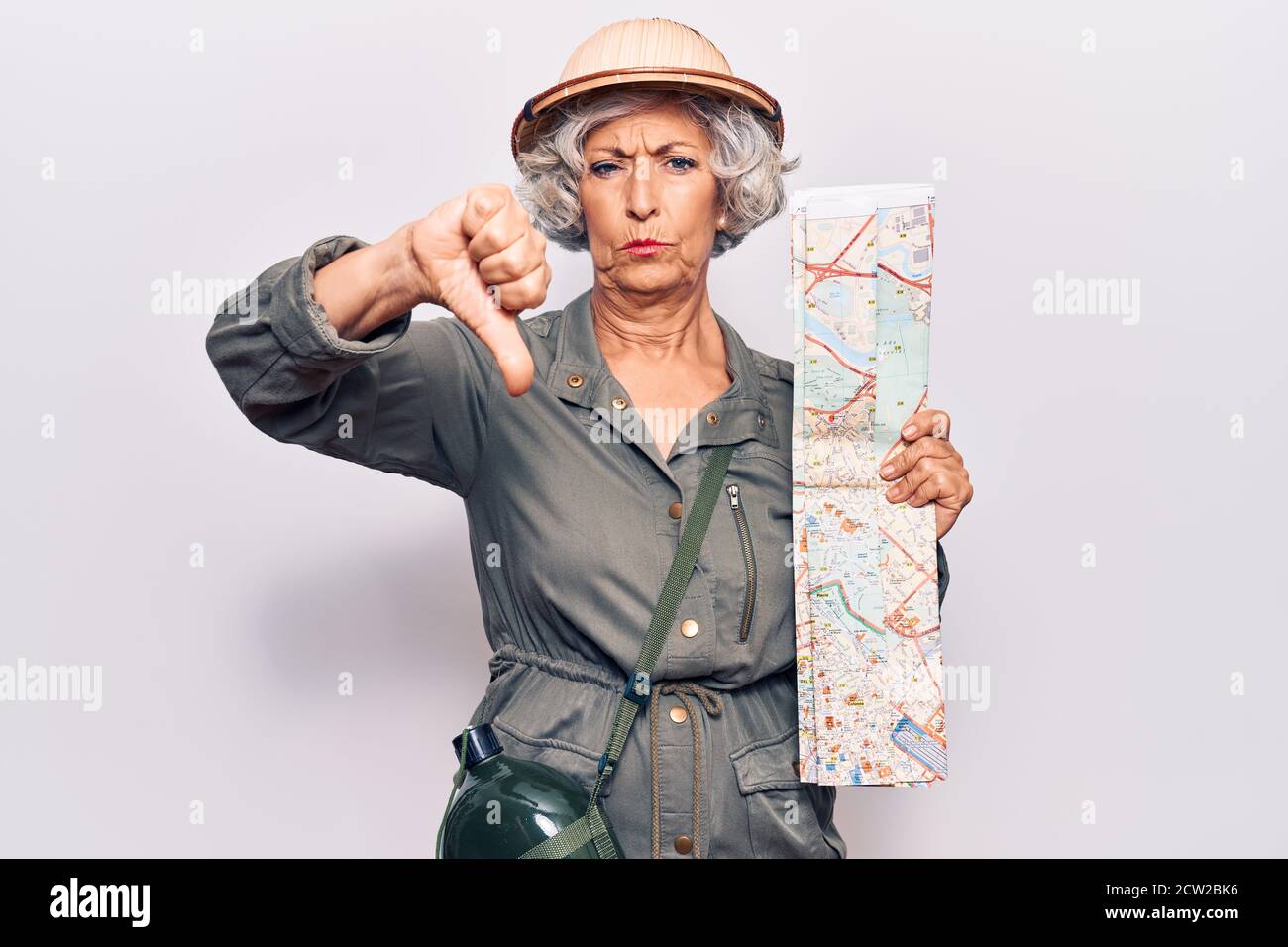 Senior grey-haired woman wearing explorer hat holding map with angry ...