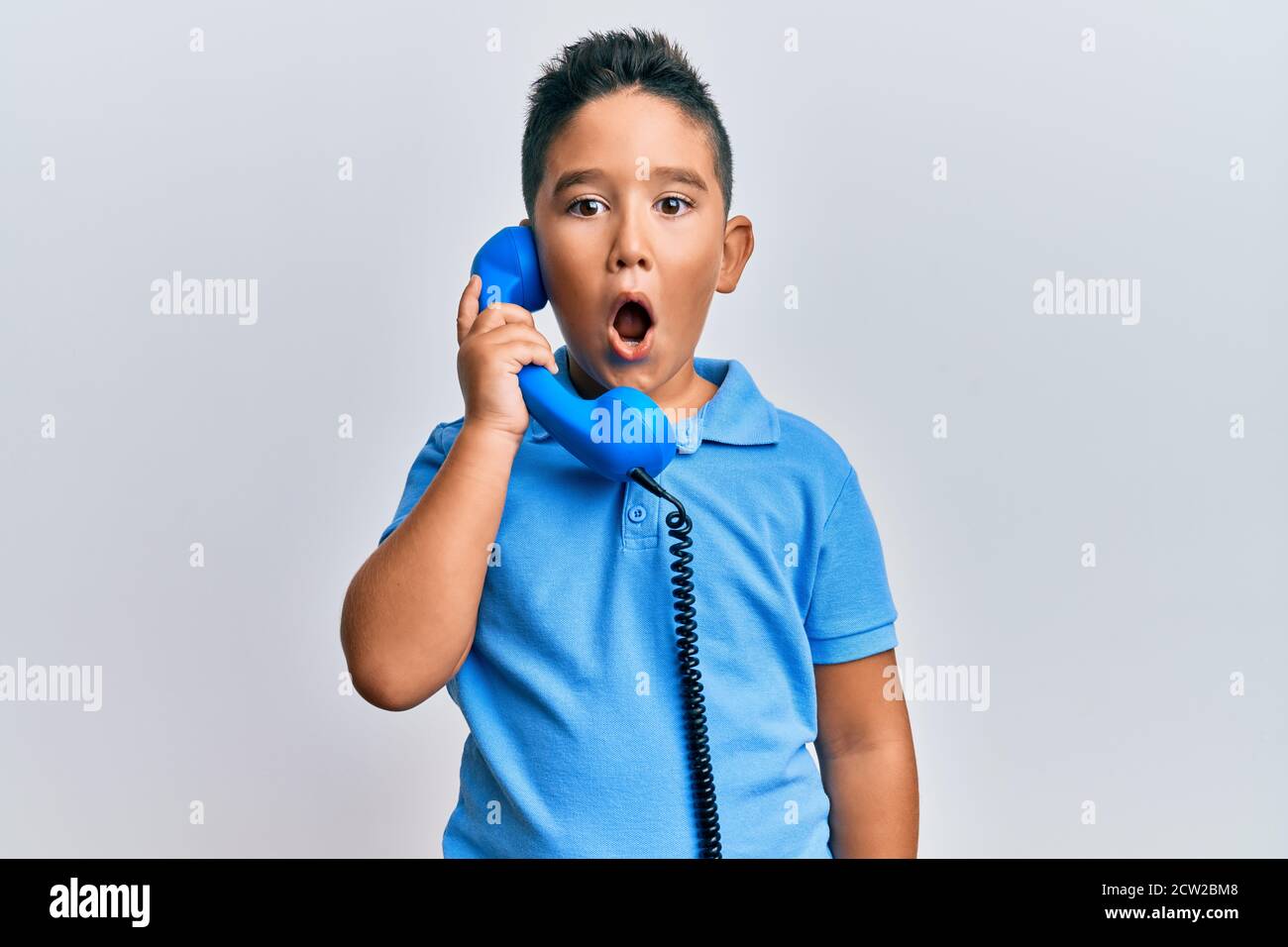 Little boy hispanic kid talking through vintage telephone scared and ...