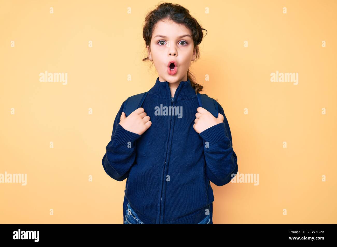 Cute hispanic child holding student backpack scared and amazed with ...