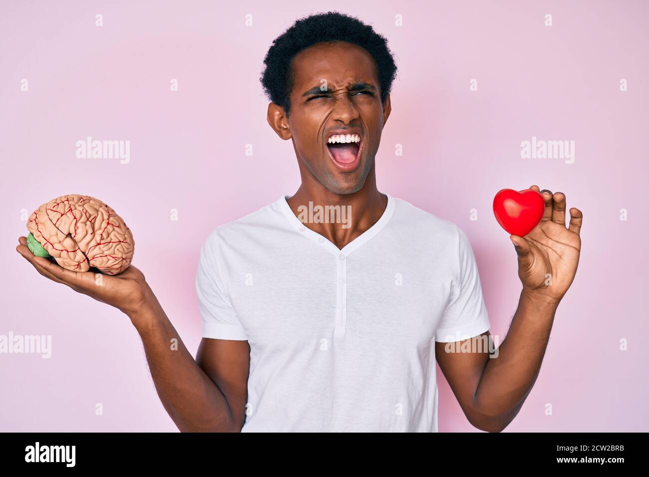 Handsome african man holding brain and heart angry and mad screaming ...