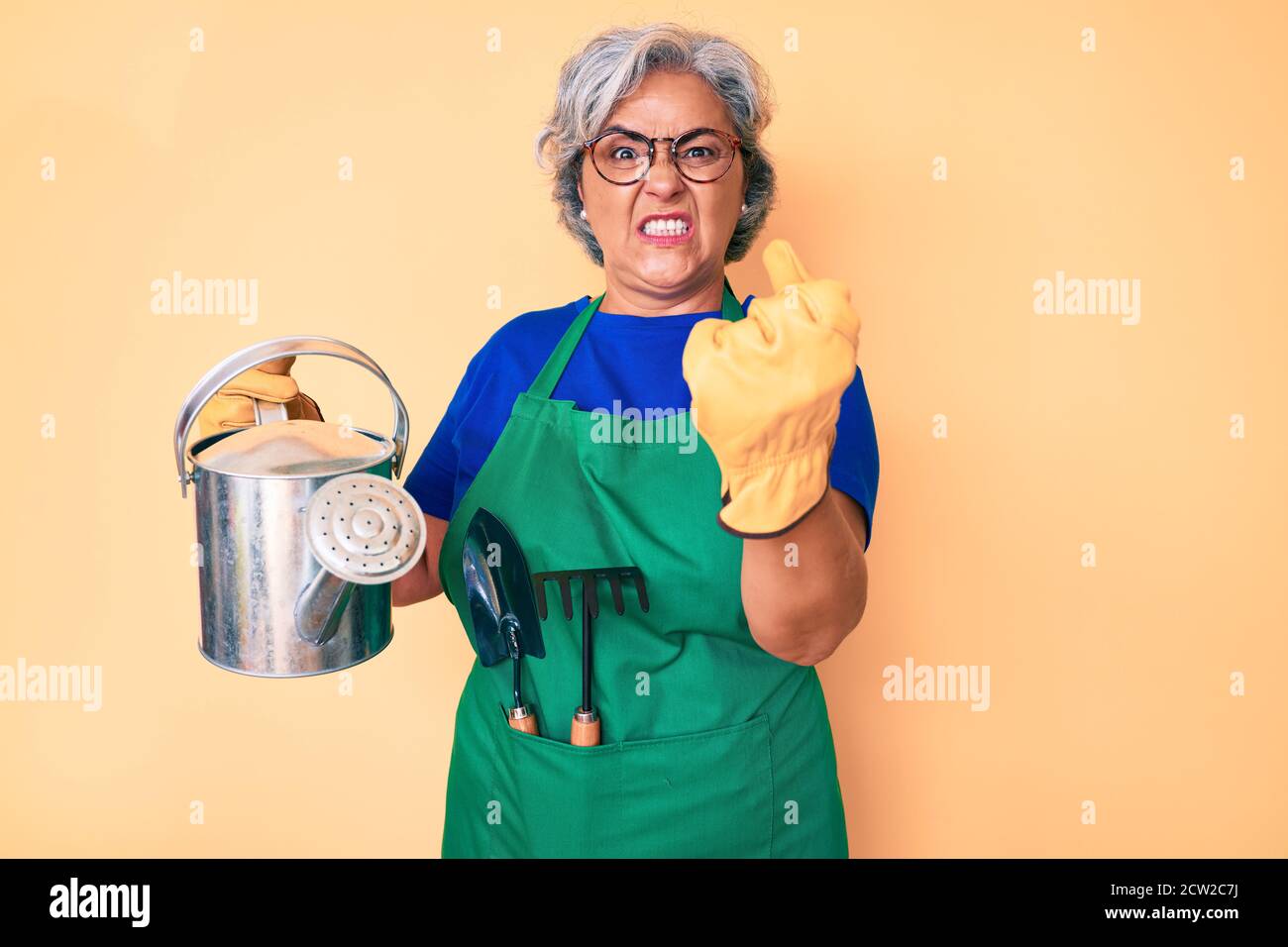 Senior hispanic grey- haired woman wearing gardener apron and gloves ...