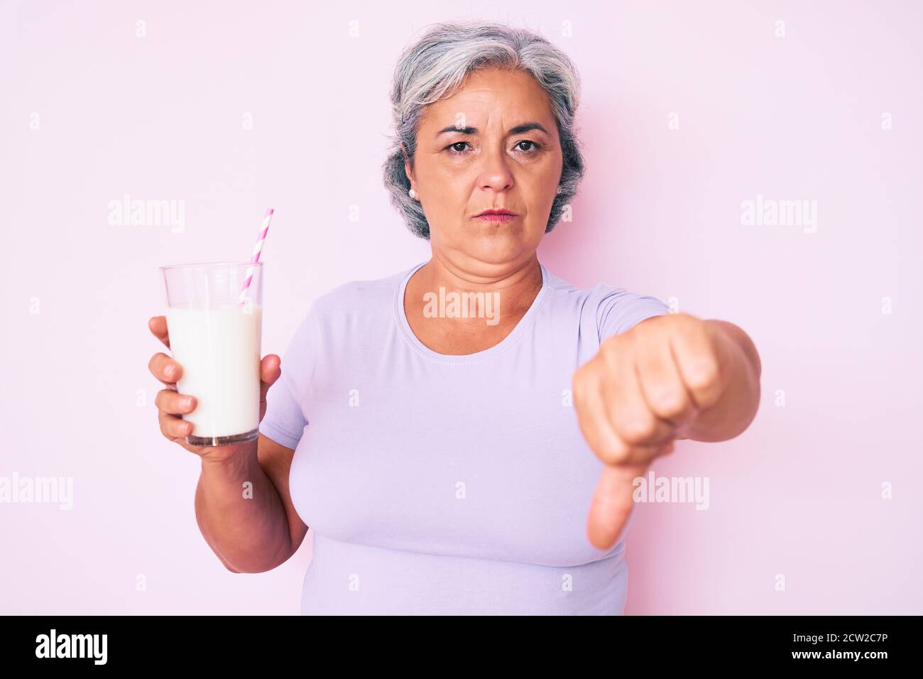 Senior hispanic woman holding glass of milk with angry face, negative ...