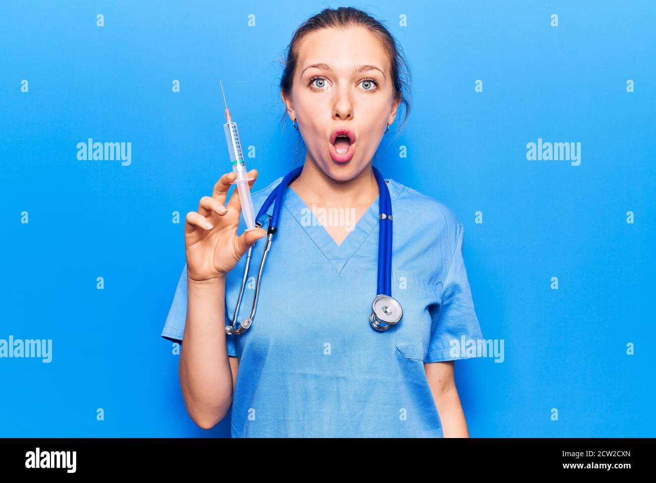 Young blonde woman wearing doctor uniform holding syringe scared and ...