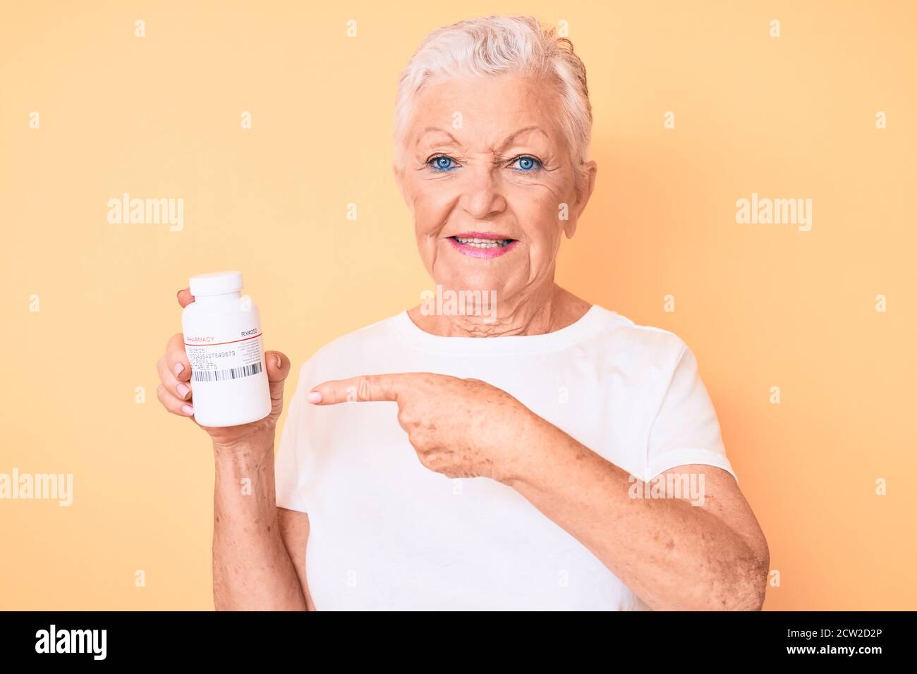 Senior beautiful woman with blue eyes and grey hair holding pills ...