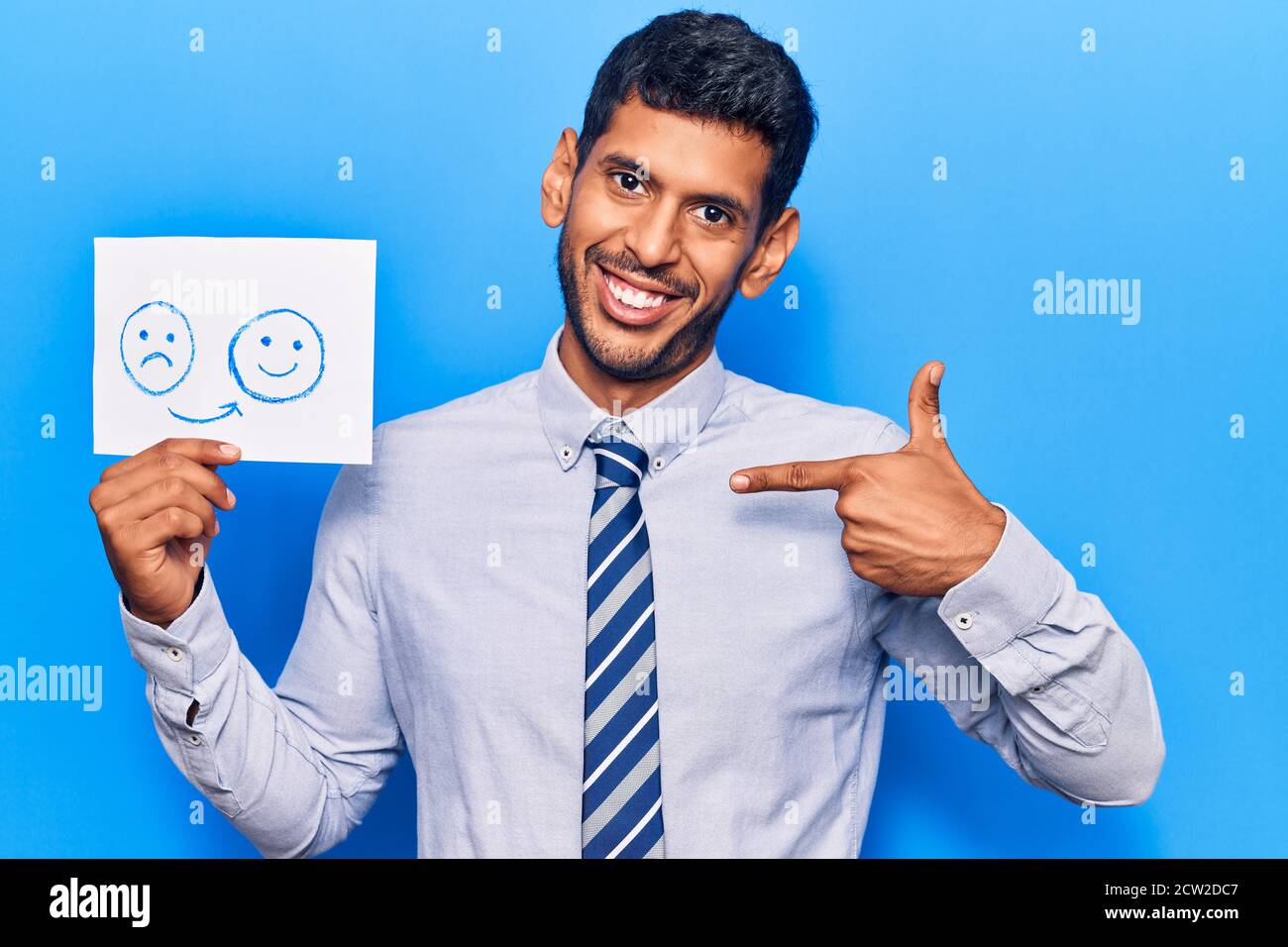 Young latin man holding sad to happy emotion paper pointing finger to ...