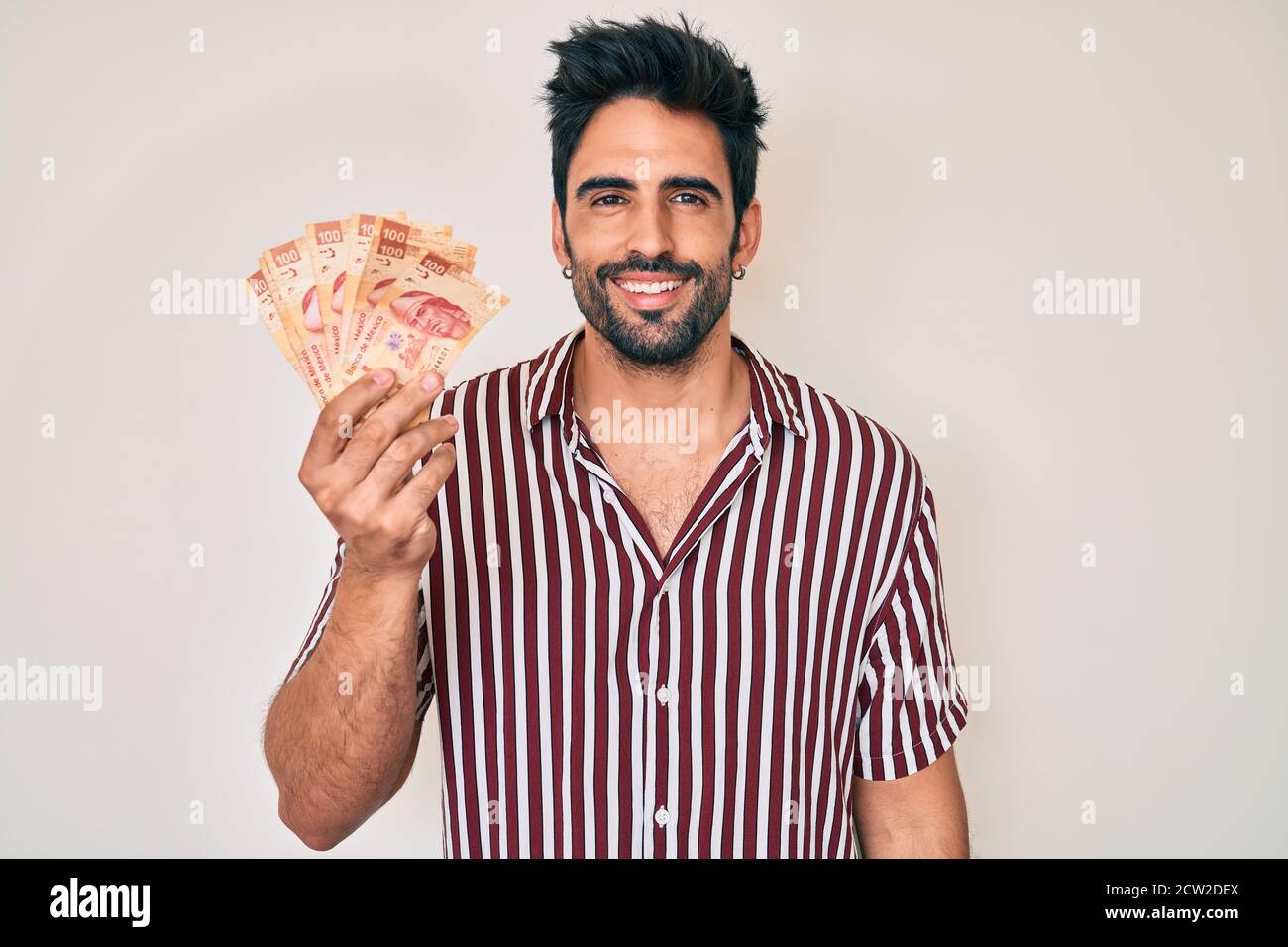 Handsome hispanic man with beard holding mexican pesos looking positive ...