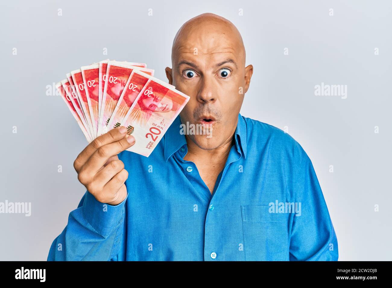 Middle age bald man holding 20 israel shekels banknotes scared and ...