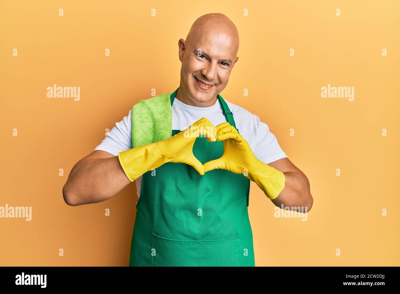 Middle age bald man wearing apron holding cleaning gloves smiling in ...