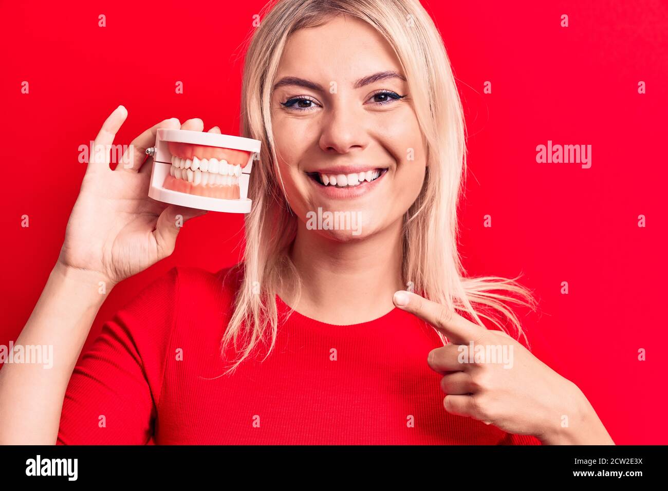 Young beautiful blonde woman holding denture teeth standing over ...