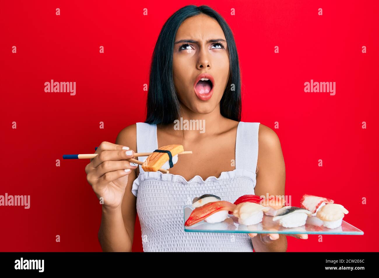 Young brunette woman eating omelet sushi using chopsticks angry and mad ...