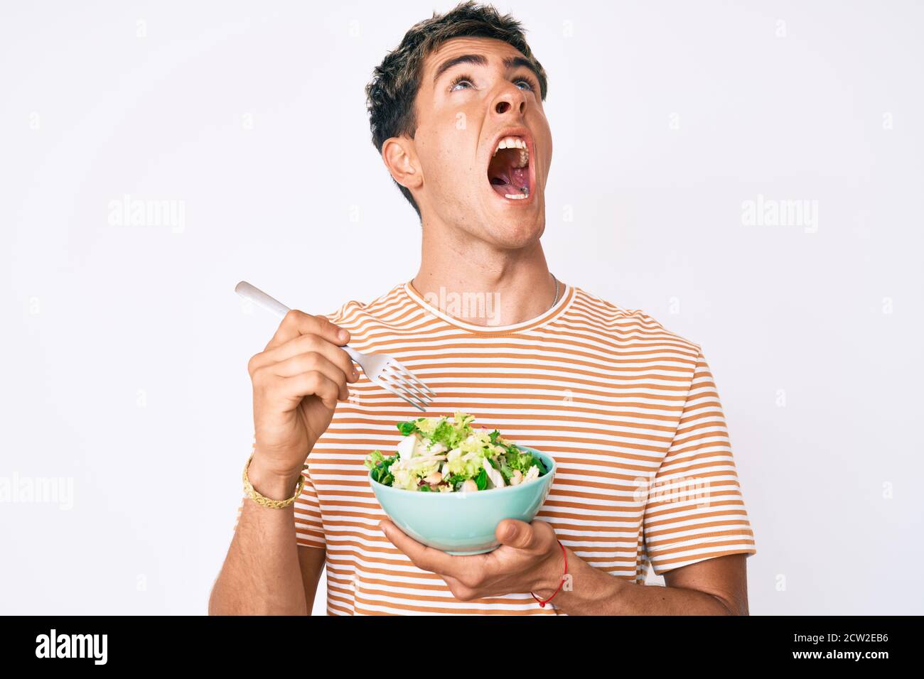 Young handsome man eating salad angry and mad screaming frustrated and ...