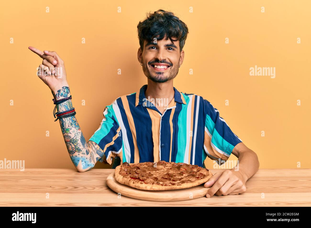 Young hispanic man eating italian pizza sitting on the table smiling ...