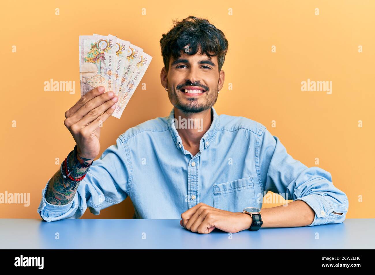 Young hispanic man holding united kingdom 10 pounds banknotes sitting ...