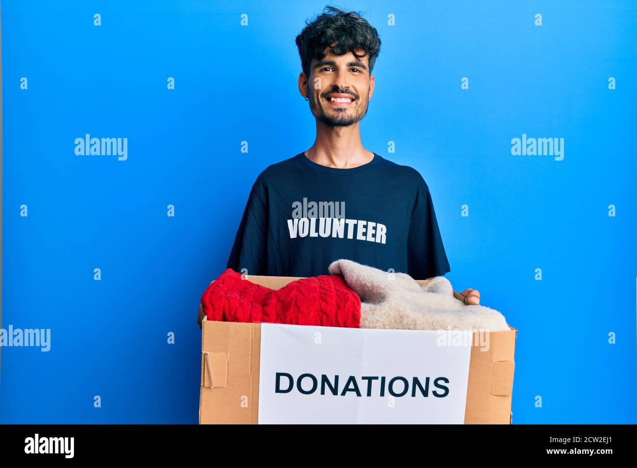 Young hispanic man holding donation box with clothes smiling with a ...