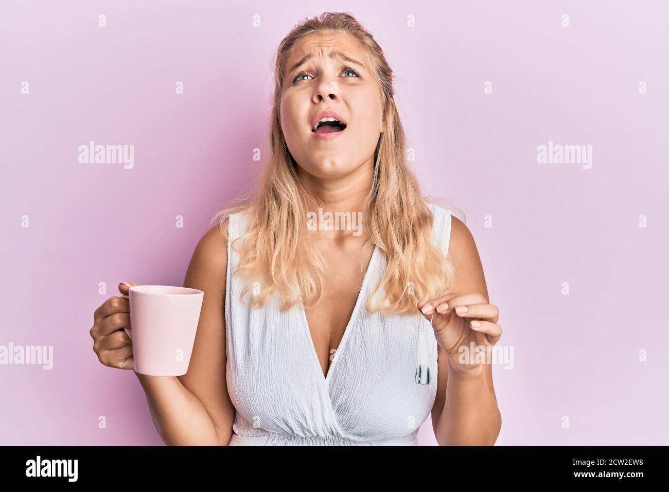 Young blonde girl holding cup of tea angry and mad screaming frustrated ...