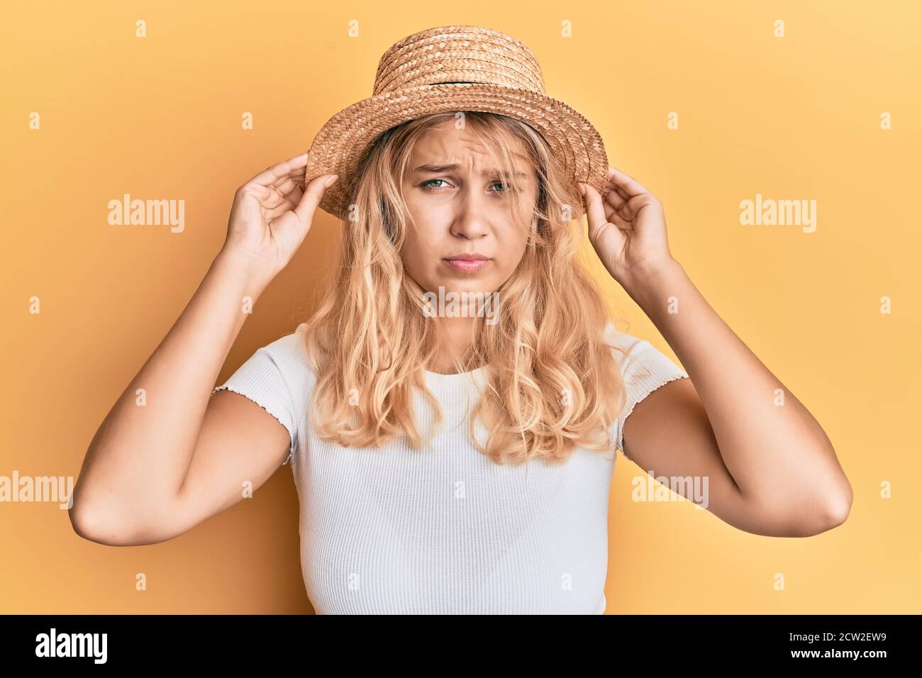Young blonde girl wearing summer hat skeptic and nervous, frowning ...