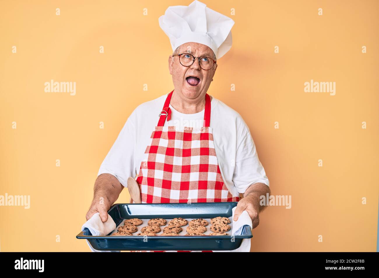 Senior grey-haired man wearing baker uniform holding homemade cookies ...