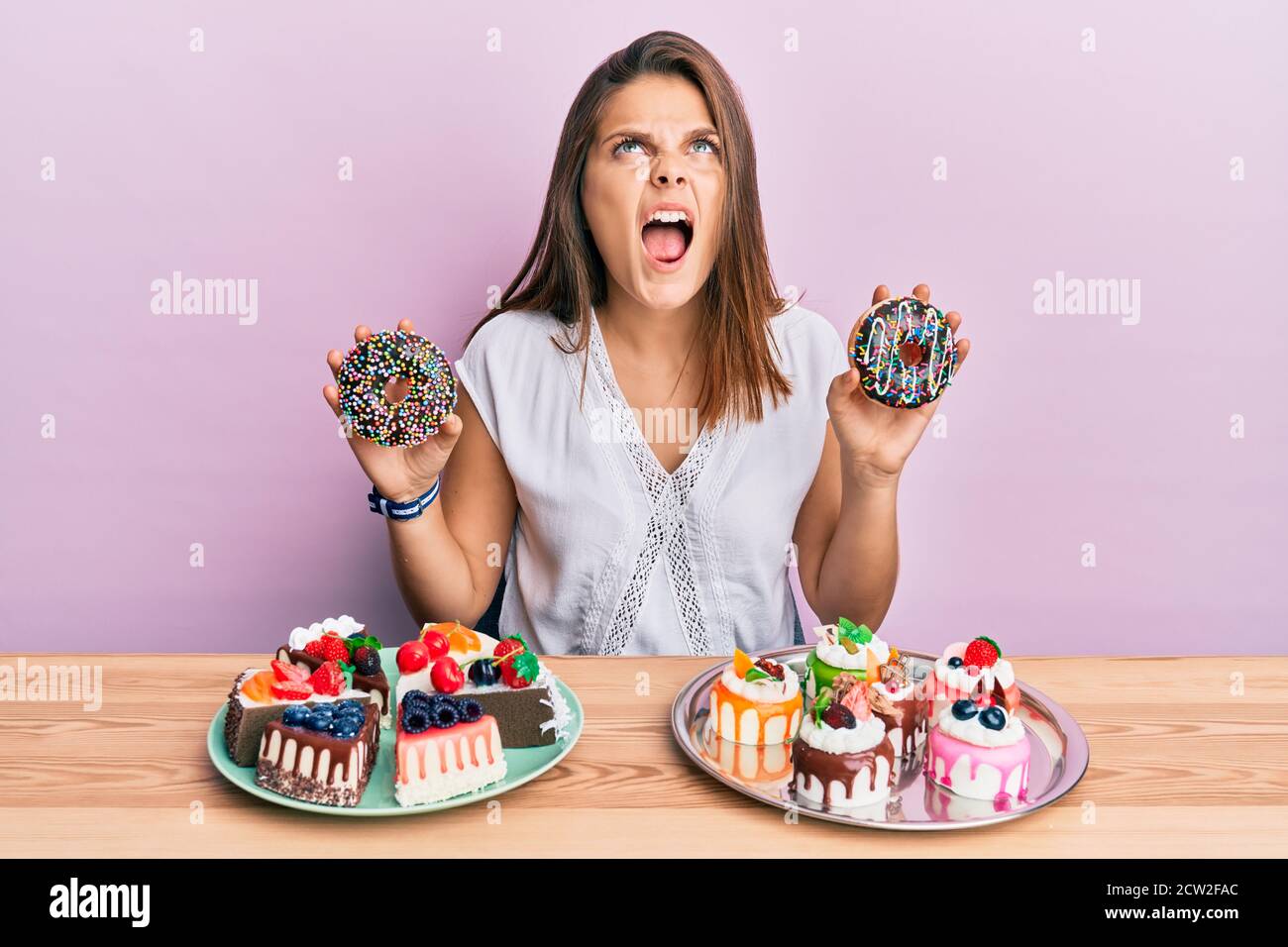 Young caucasian woman eating pastries for breakfast angry and mad ...