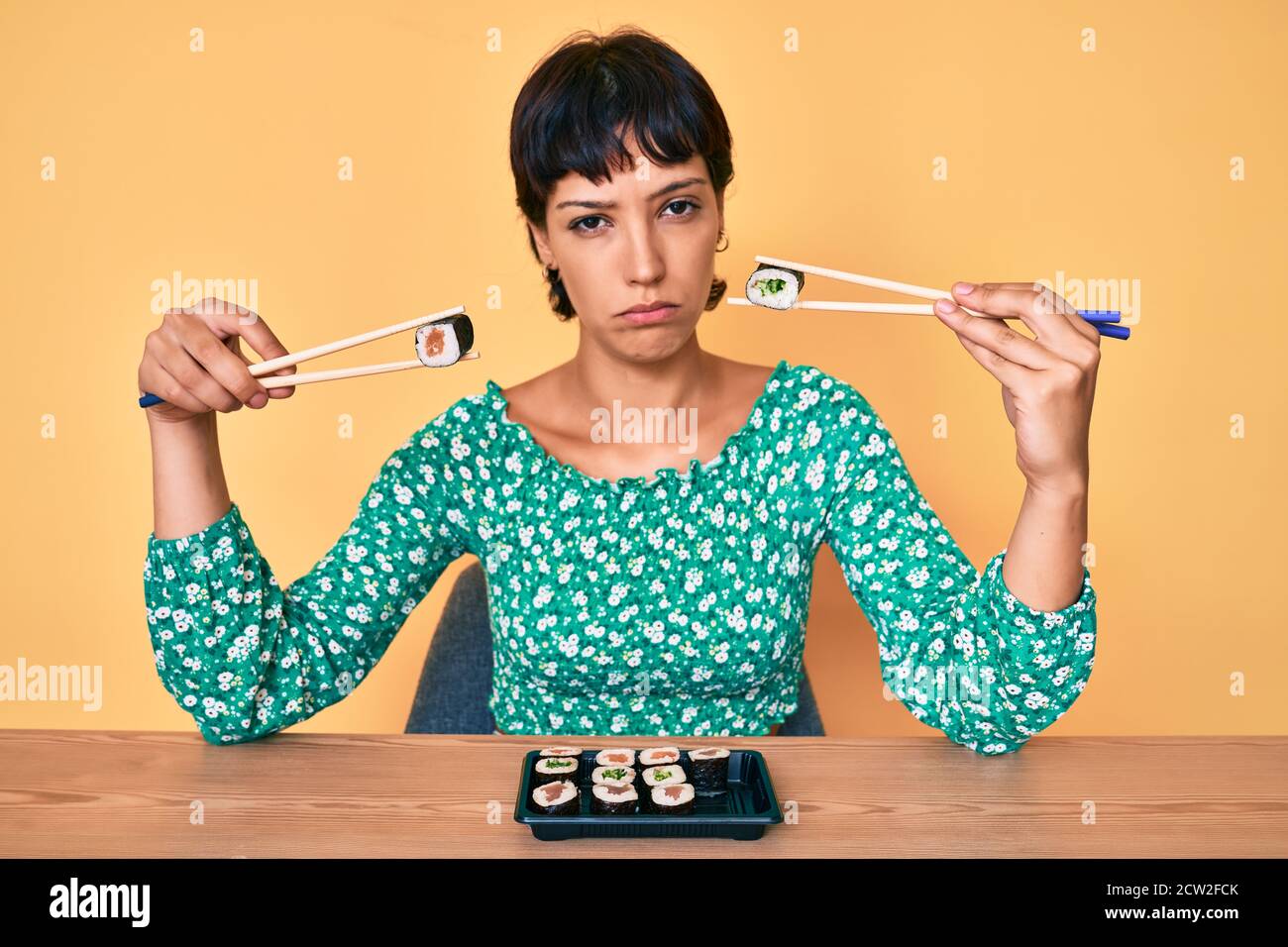 Beautiful brunettte woman eating sushi sitting on the table depressed ...