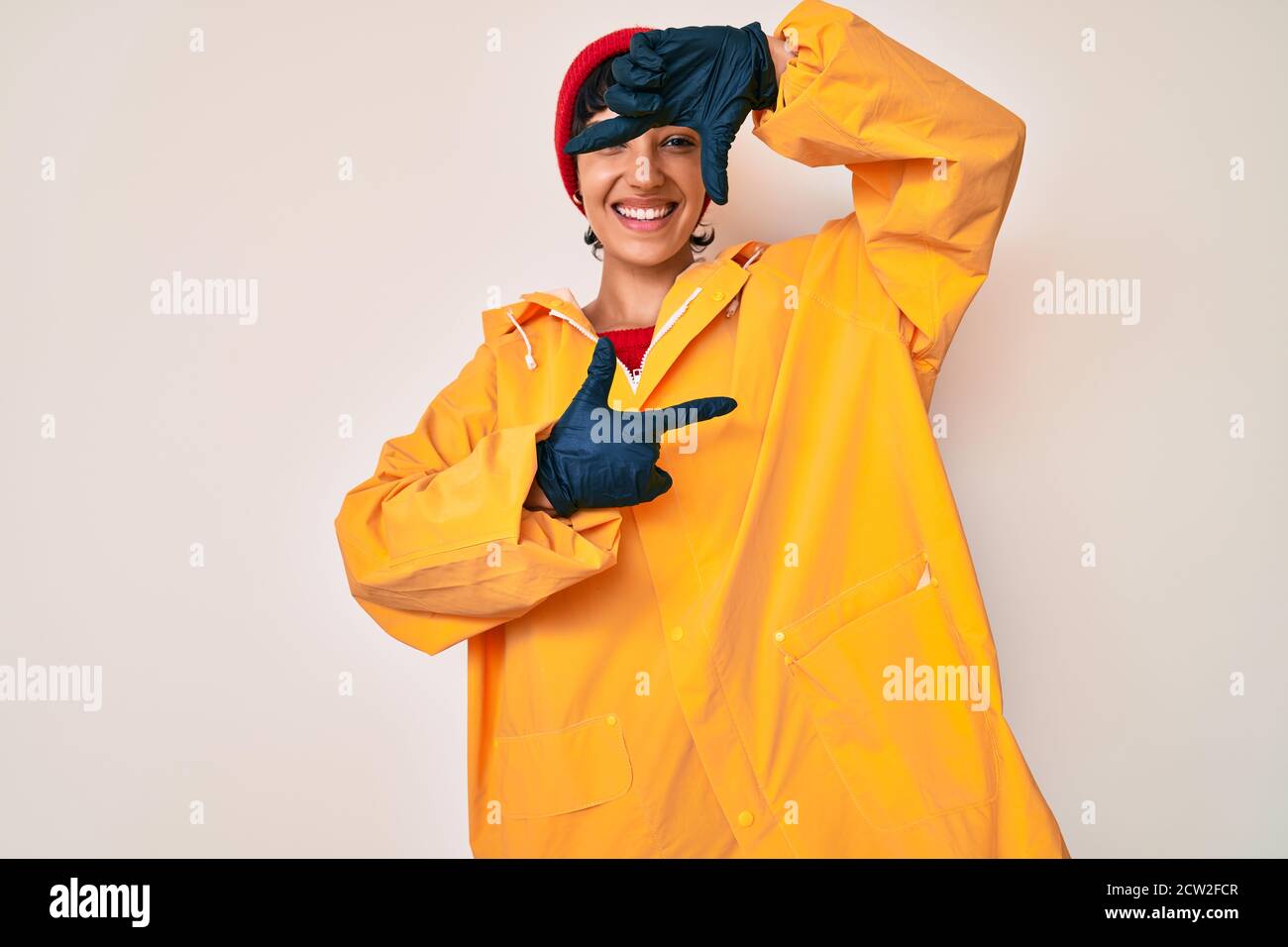 Beautiful brunettte woman wearing yellow raincoat smiling making frame ...