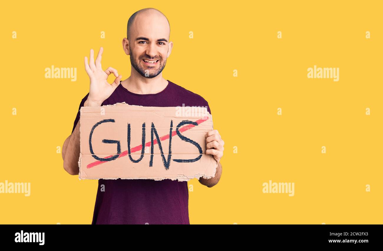 Young handsome man holding prohibited guns banner doing ok sign with ...