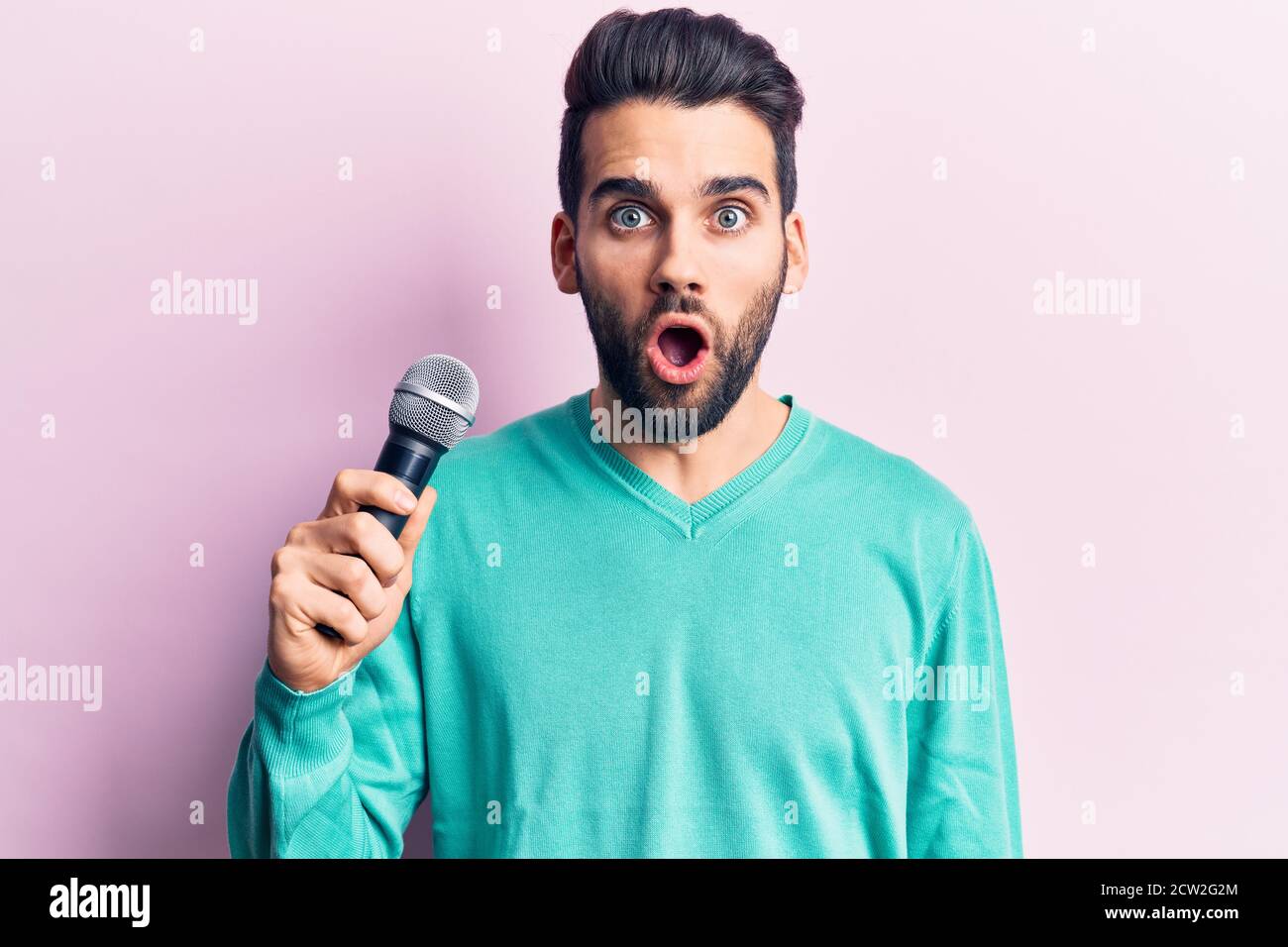 Young handsome man with beard singing song using microphone scared and ...
